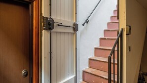 Uma porta de madeira com puxador de metal, uma porta deslizante branca com puxador de metal, e uma escada com degraus vermelhos e corrimão preto.