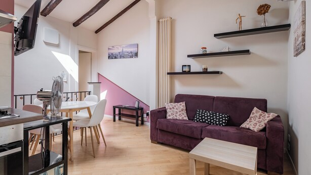Uma sala de estar moderna com um sofá roxo, piso de madeira e uma pintura da paisagem urbana na parede.