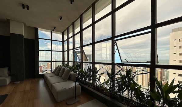 Uma sala de estar moderna com uma janela grande, um sofá e um arranjo de plantas.