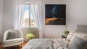 Quarto com cama, cadeira, pôster de céu noturno, janela com cortinas e radiador.