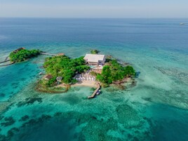 Vista aérea de uma ilha tropical com um grande edifício rodeado por vegetação exuberante e águas azul-claras.