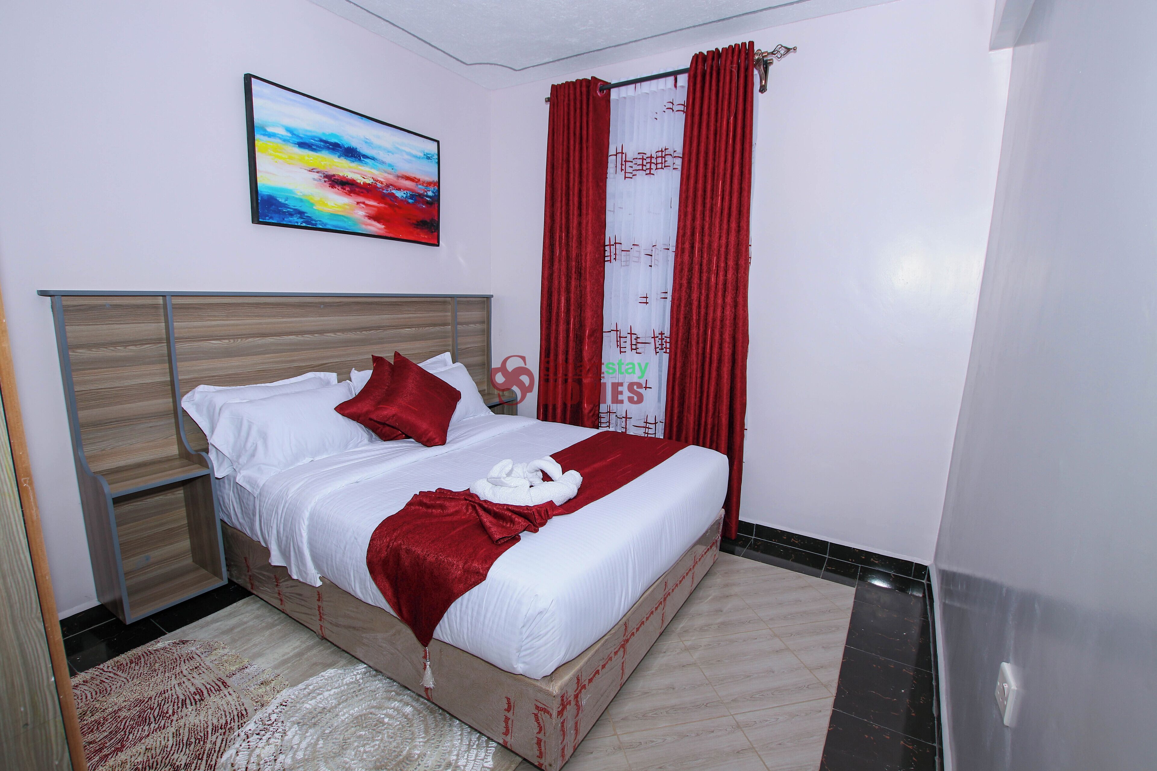 Cama bem arrumada com roupa de cama branca e vermelha, um cobertor vermelho e uma toalha branca.