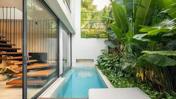 Uma área de piscina moderna ao ar livre, com deck de madeira, paredes de vidro e vegetação tropical exuberante.