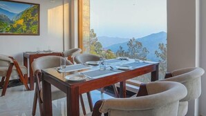 Uma sala de jantar com uma mesa posta para quatro pessoas, grandes janelas com vista para as montanhas e um quadro na parede.