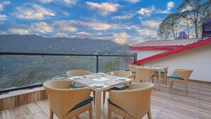 Terraço com mobiliário de vime e mesa posta para refeições, com vista para uma paisagem montanhosa.