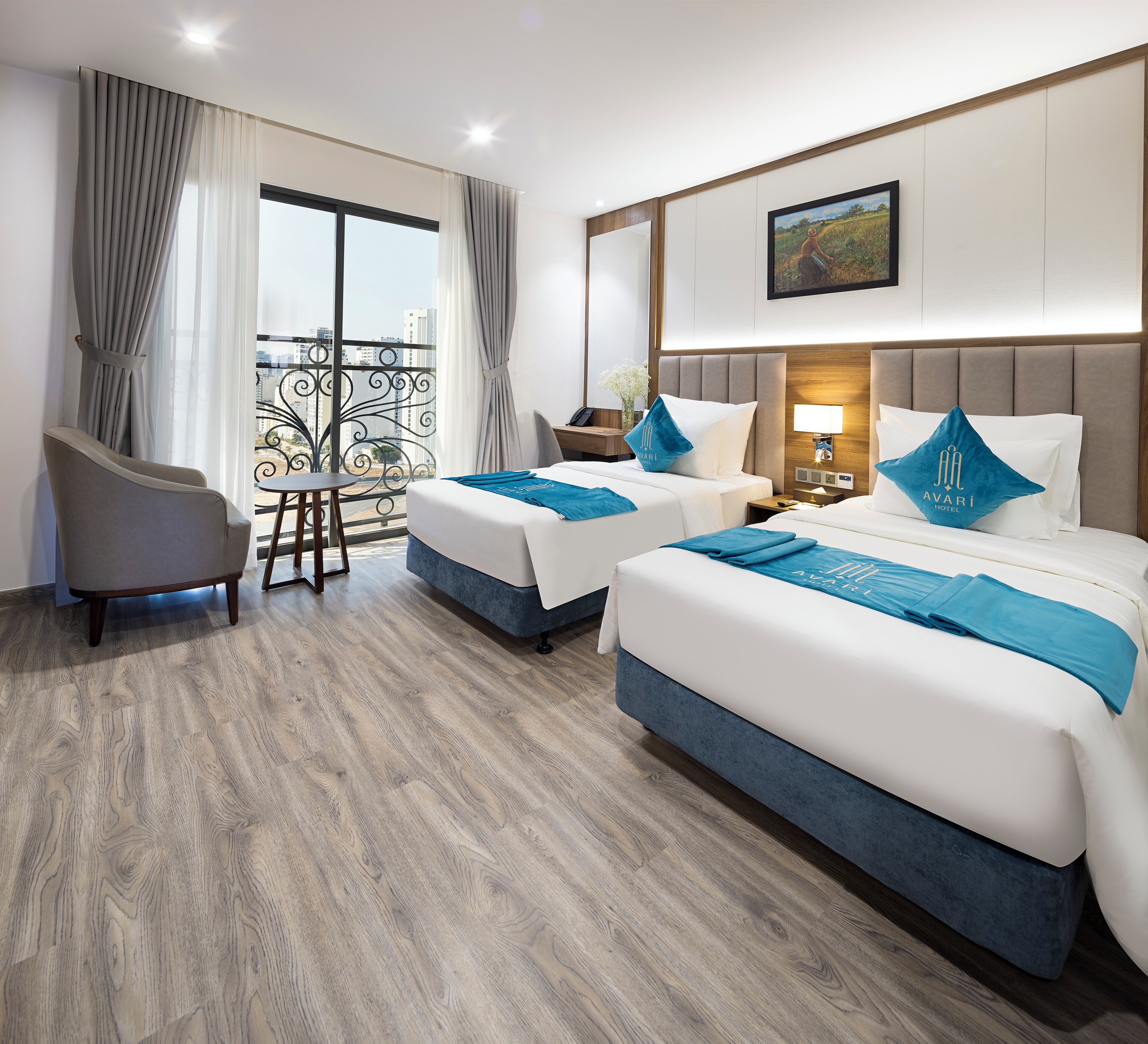 Quarto de hotel com duas camas, uma cadeira, varanda com vista e um quadro na parede.