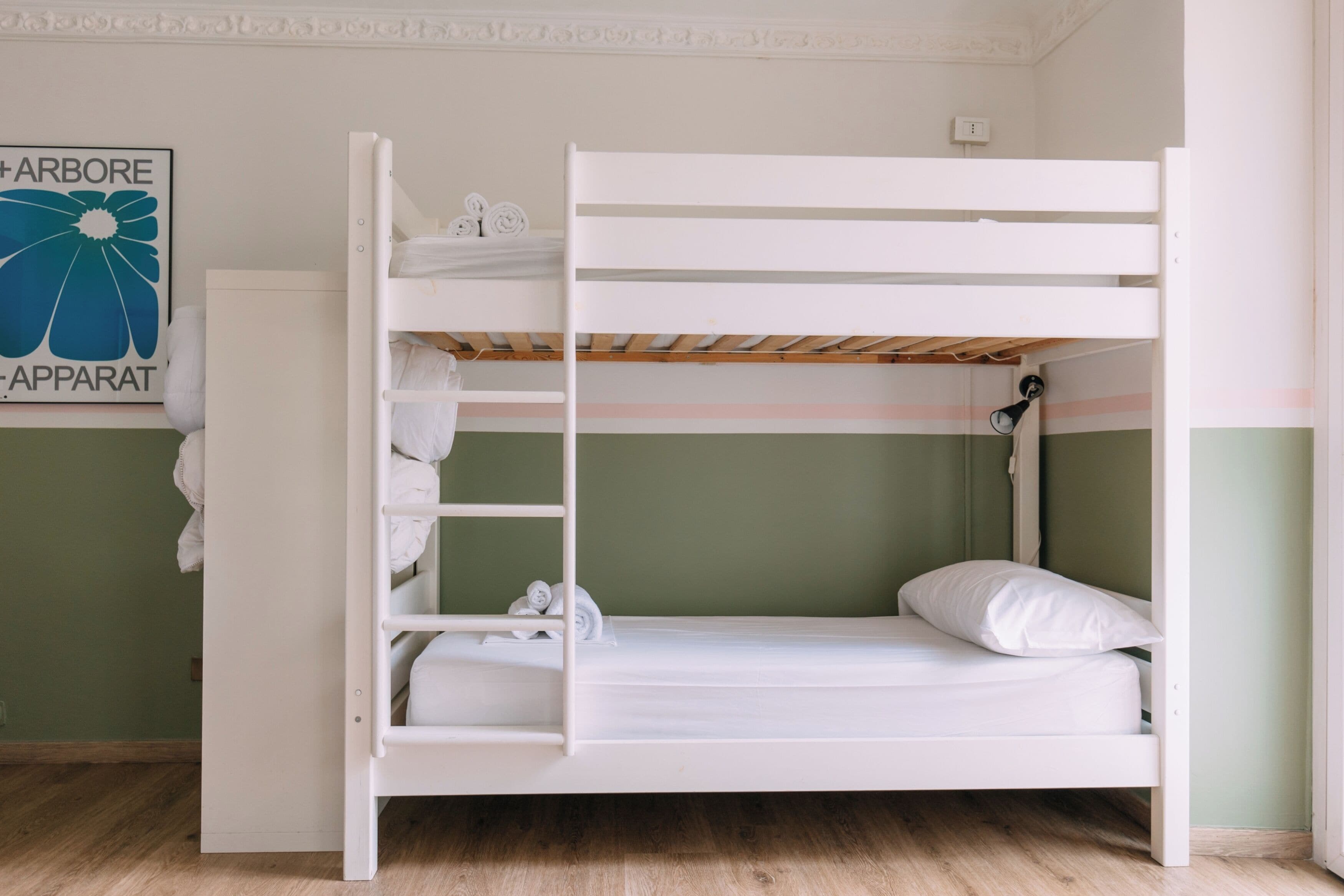 Uma cama de solteiro com roupa de cama branca e uma pequena prateleira em cima.