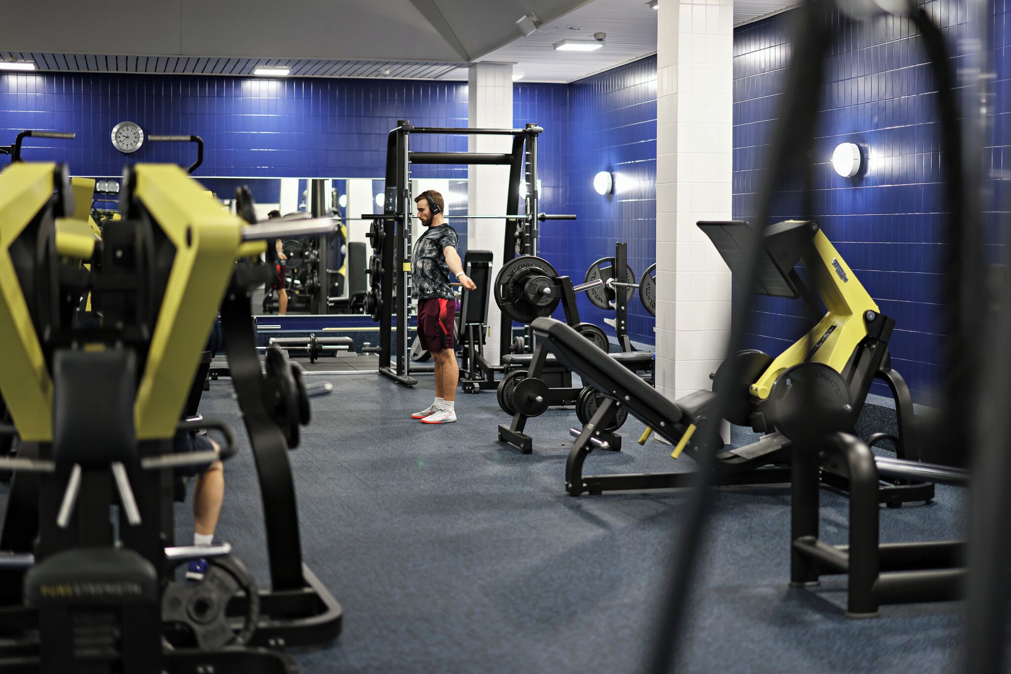 Uma academia com paredes azuis, equipamentos de musculação e um relógio na parede.