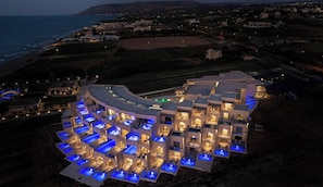 Hotel moderno com várias varandas e piscinas, situado perto de uma praia.