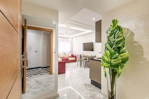 Uma sala de estar moderna com sofá, mesa de jantar e cadeiras. Há uma planta grande no canto.