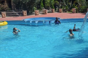 Piscina com água azul cristalina, uma bóia amarela e um deck de pedra com bancos.