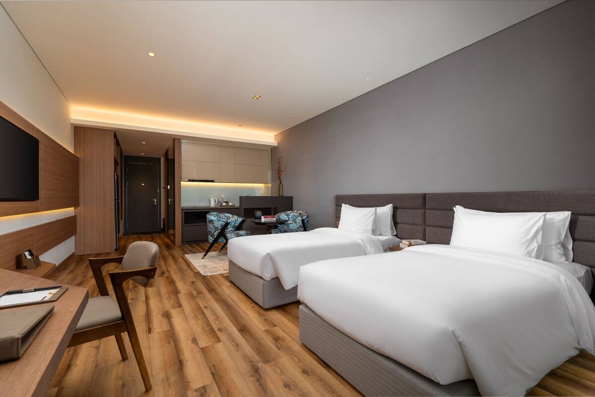 Quarto de hotel moderno com duas camas, uma escrivaninha e um espaço de estar.