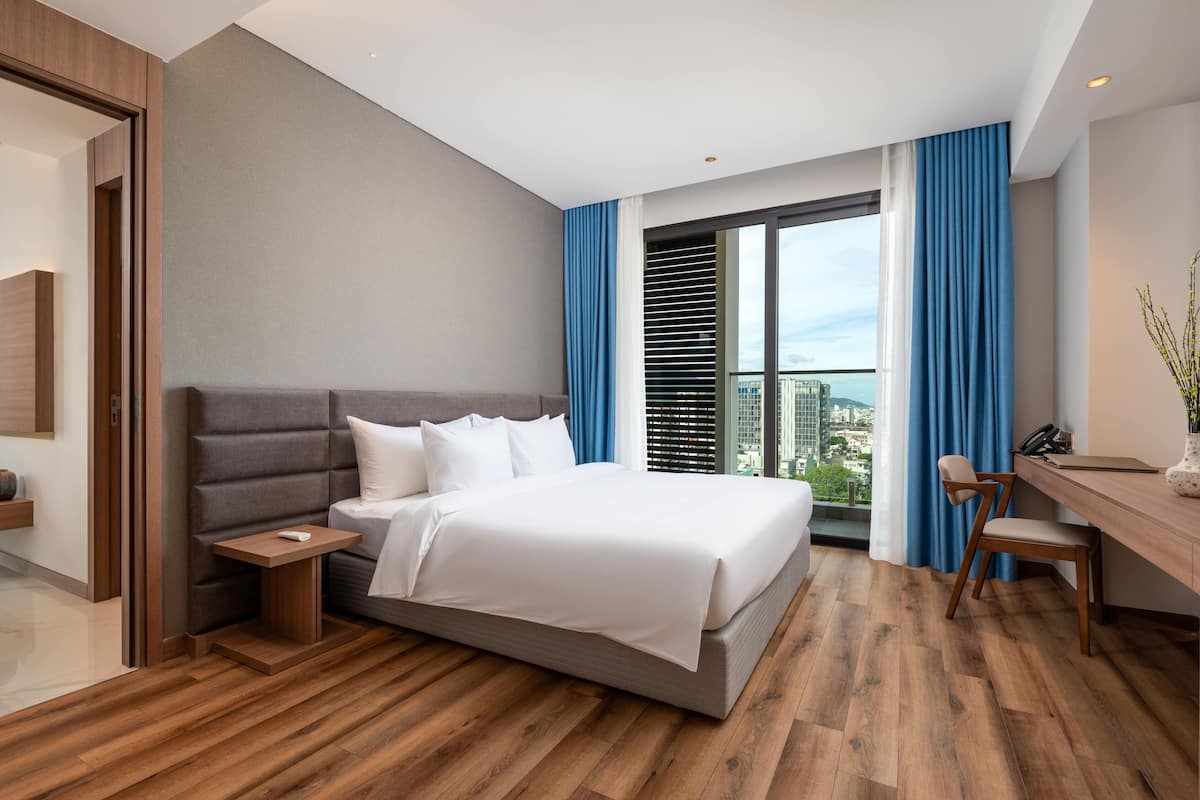 Quarto de hotel moderno com uma cama grande, uma escrivaninha e vista para a cidade.