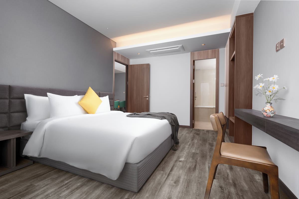 Quarto de hotel moderno com uma cama grande, uma cadeira de madeira, uma escrivaninha e um vaso com flores.