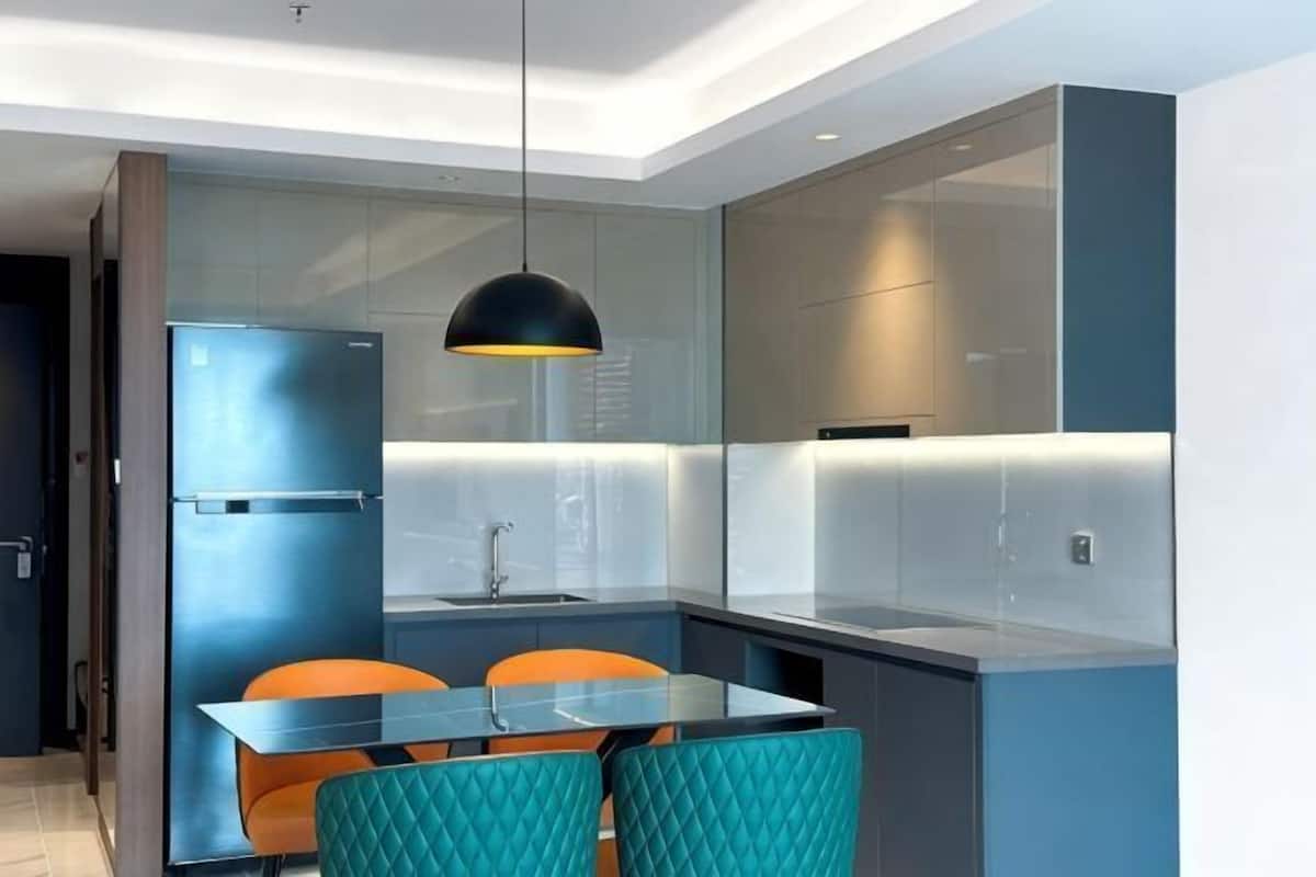 Uma cozinha moderna com uma mesa de jantar de vidro, cadeiras verde-água e uma luminária pendente preta.