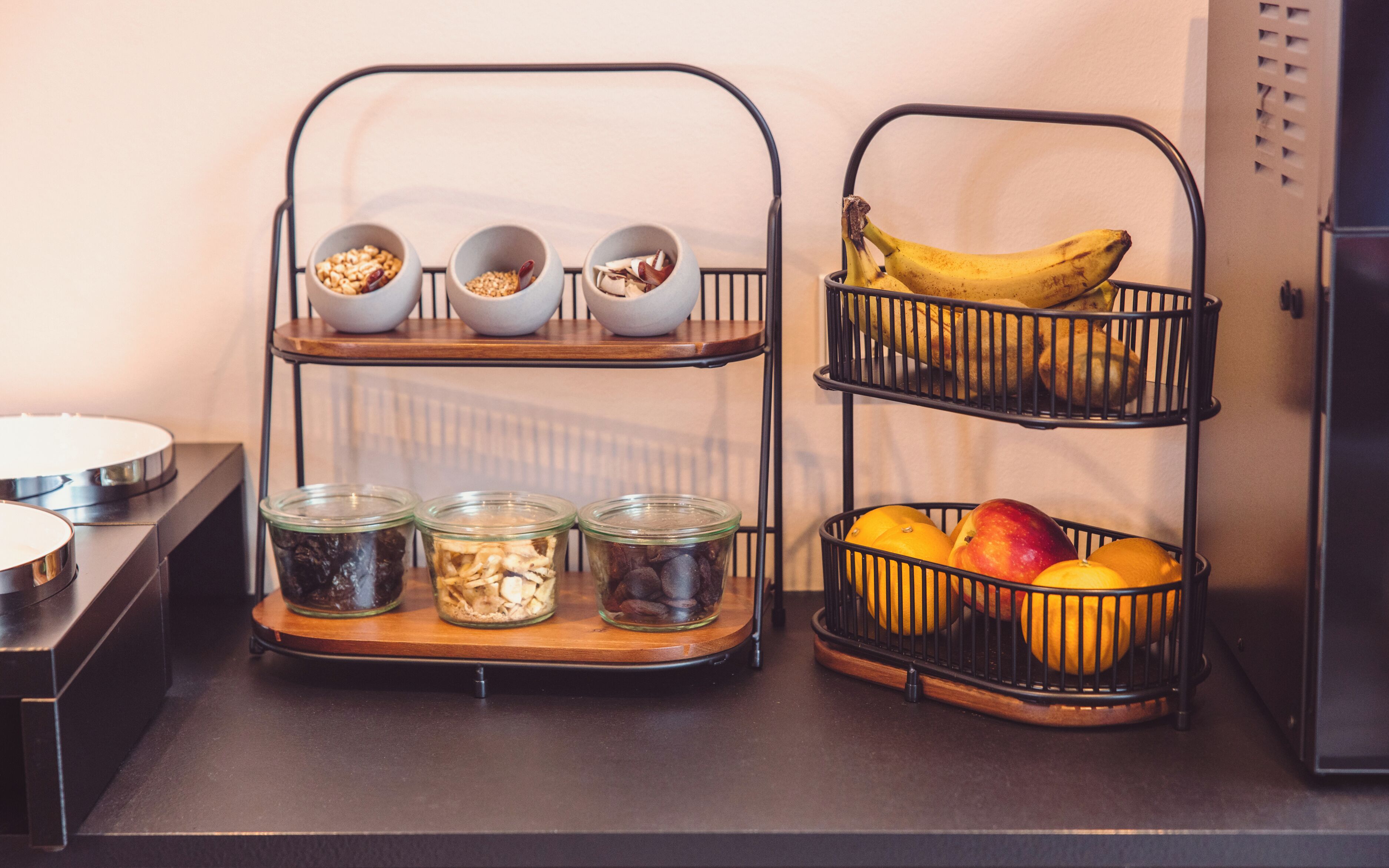 Uma cozinha compacta com uma estante de metal contendo uma banana e maçãs, e três potes de vidro sobre uma bandeja de madeira.
