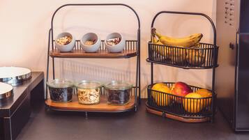 Uma cozinha compacta com uma estante de metal contendo uma banana e maçãs, e três potes de vidro sobre uma bandeja de madeira.