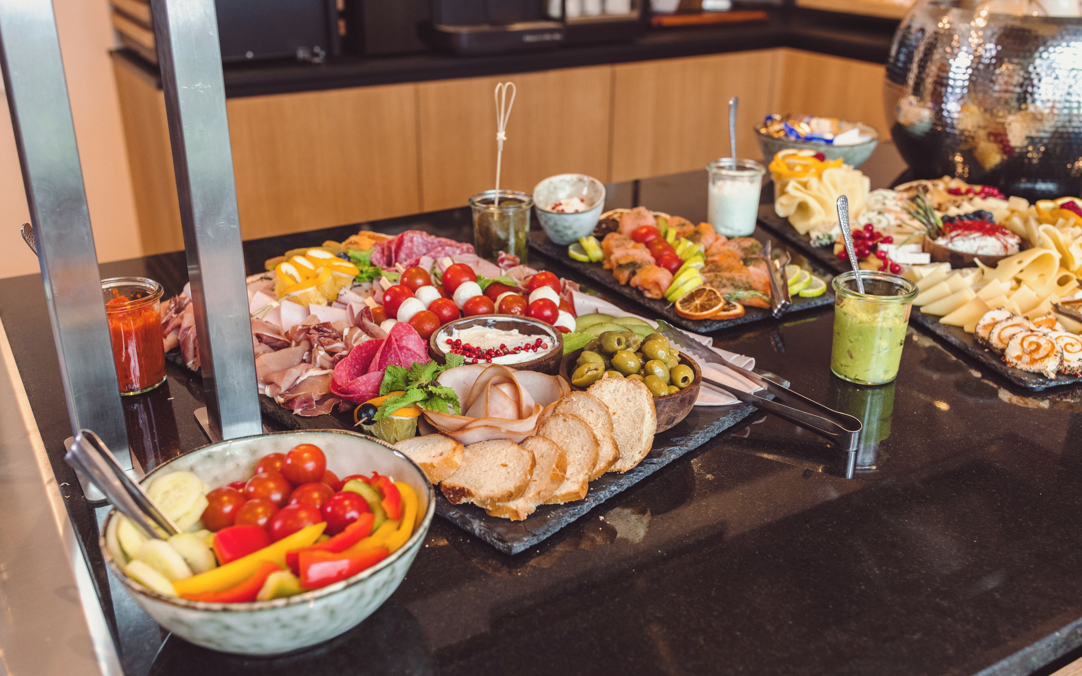 Uma mesa de buffet com diversos alimentos, incluindo carnes, queijos, frutas e legumes.