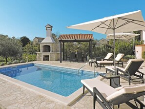 Piscina com espreguiçadeiras e espaço para churrasco.