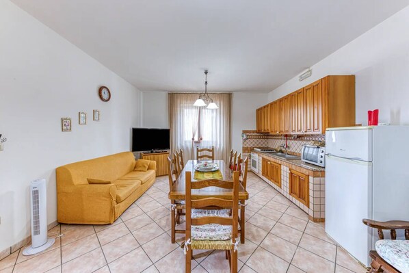 Espaço compacto com mesa de jantar, sofá, cozinha e televisão.