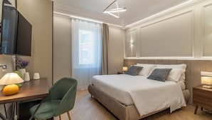 Quarto de hotel moderno com cama, mesa de cabeceira, luminária, cadeira e televisão.