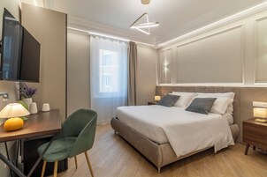 Quarto de hotel moderno com cama, mesa de cabeceira, luminária, cadeira e televisão.