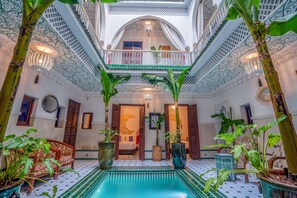 Um interior luxuoso com piscina central, teto ricamente decorado e mobiliário tradicional.