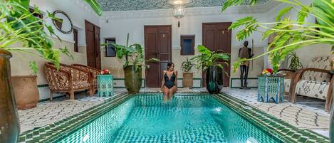 Piscina interior com piso e paredes azulejadas, cercada por mobiliário tradicional e plantas em vasos.