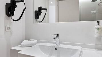Um banheiro moderno com uma pia branca, um espelho e dois secadores de cabelo fixados na parede.