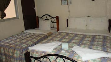 Quarto com duas camas de solteiro, cada uma com colcha estampada e travesseiro branco. Há um telefone na parede e uma porta à esquerda.