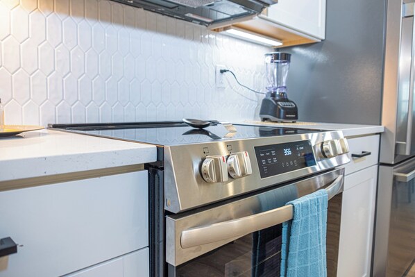Uma cozinha com forno de aço inoxidável, liquidificador e painel de azulejos brancos.