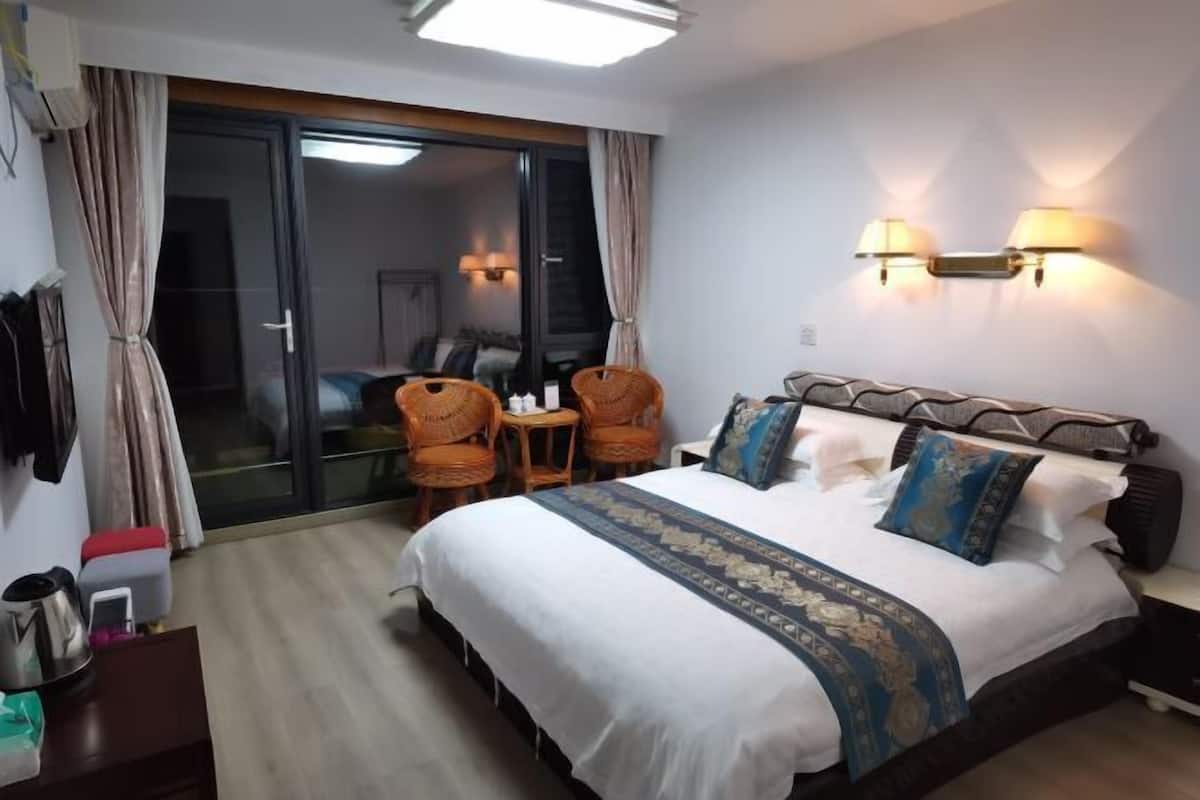 Quarto de hotel com uma cama grande, duas cadeiras, uma mesa pequena e uma porta de vidro que se abre para uma varanda.