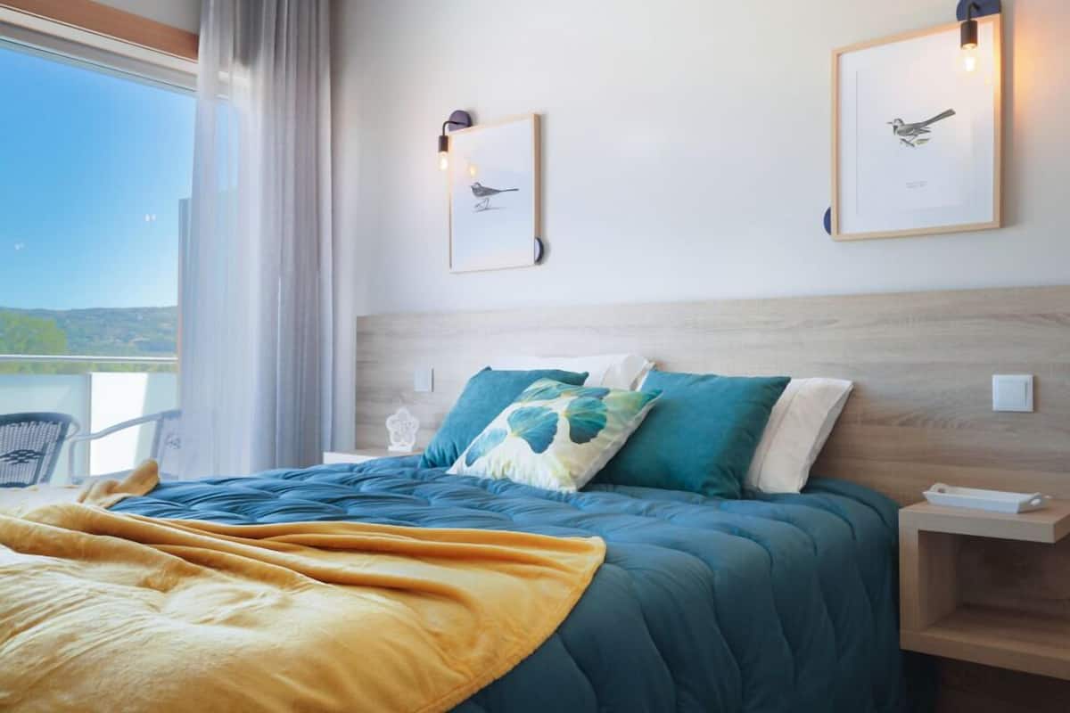 Quarto de hotel com uma cama grande, vista para o exterior e duas fotografias emolduradas na parede.