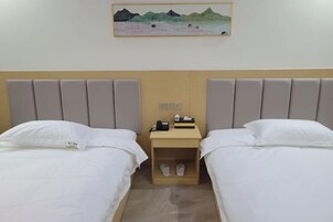 Quarto de hotel com duas camas, uma mesa de cabeceira com telefone e abajur, e um quadro na parede.
