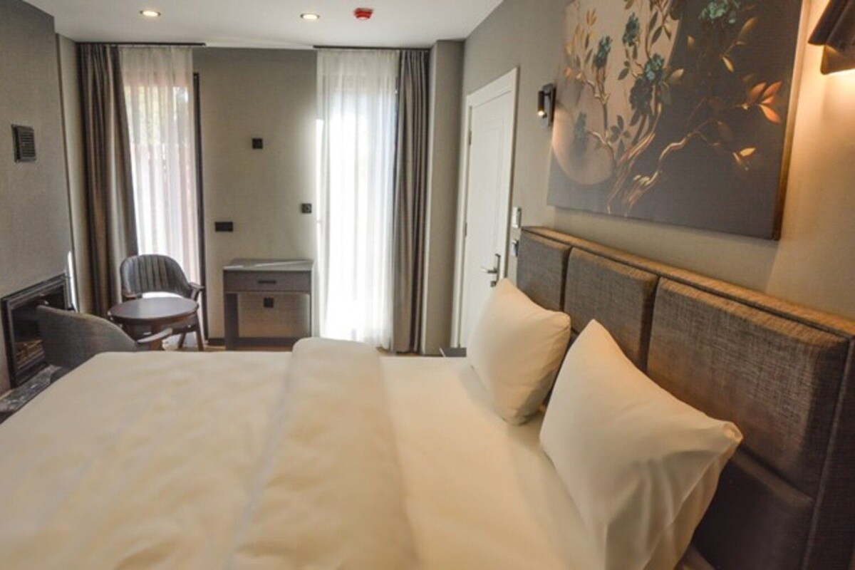 Quarto de hotel com uma cama grande, uma escrivaninha, uma cadeira e uma televisão fixada na parede.