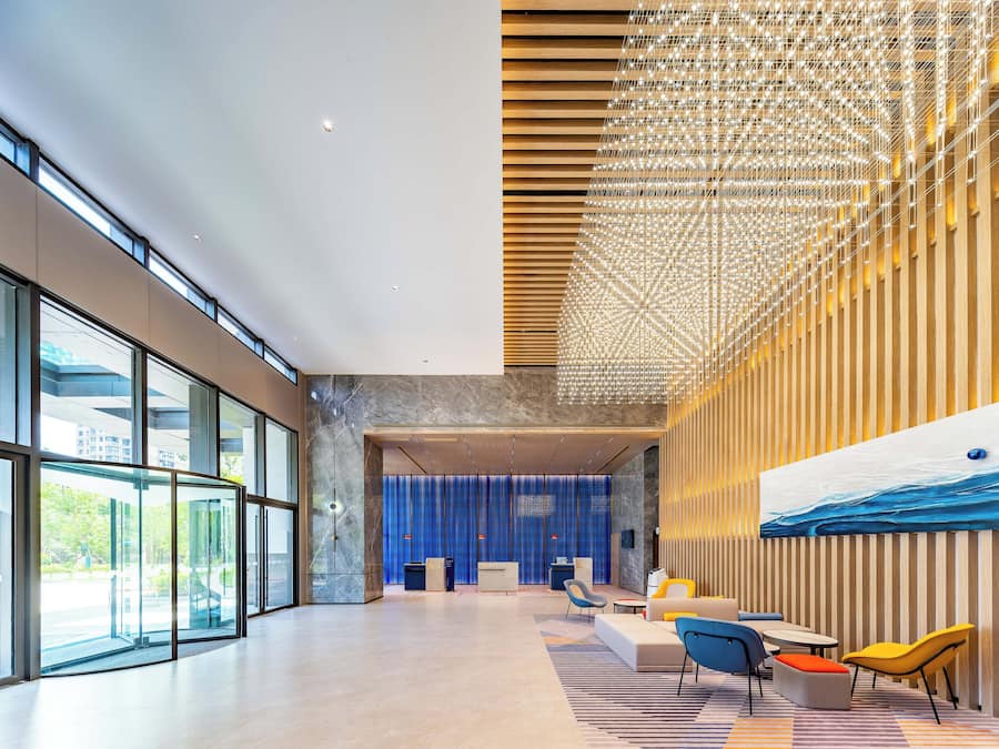 Um hall amplo com grandes janelas, um lustre moderno e uma área de estar com cadeiras coloridas.