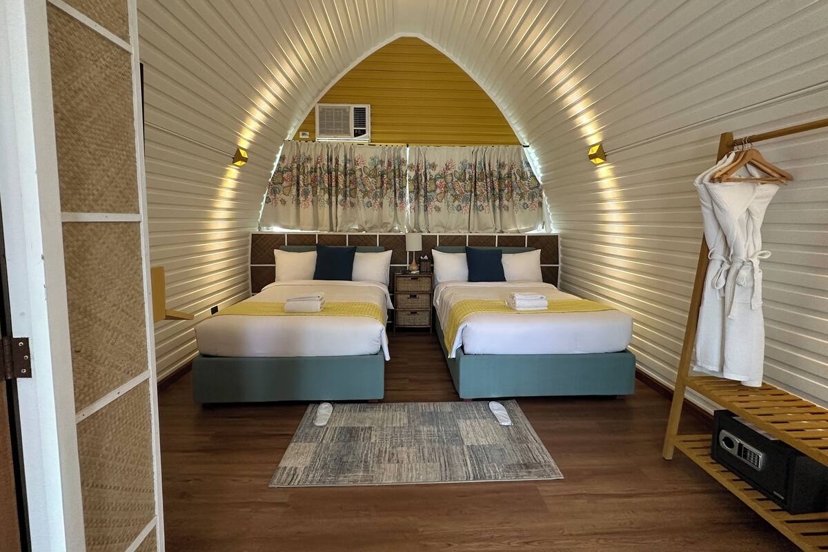 Um quarto aconchegante em arco, com duas camas, piso de madeira, roupão pendurado e uma pequena mesa com um alto-falante.