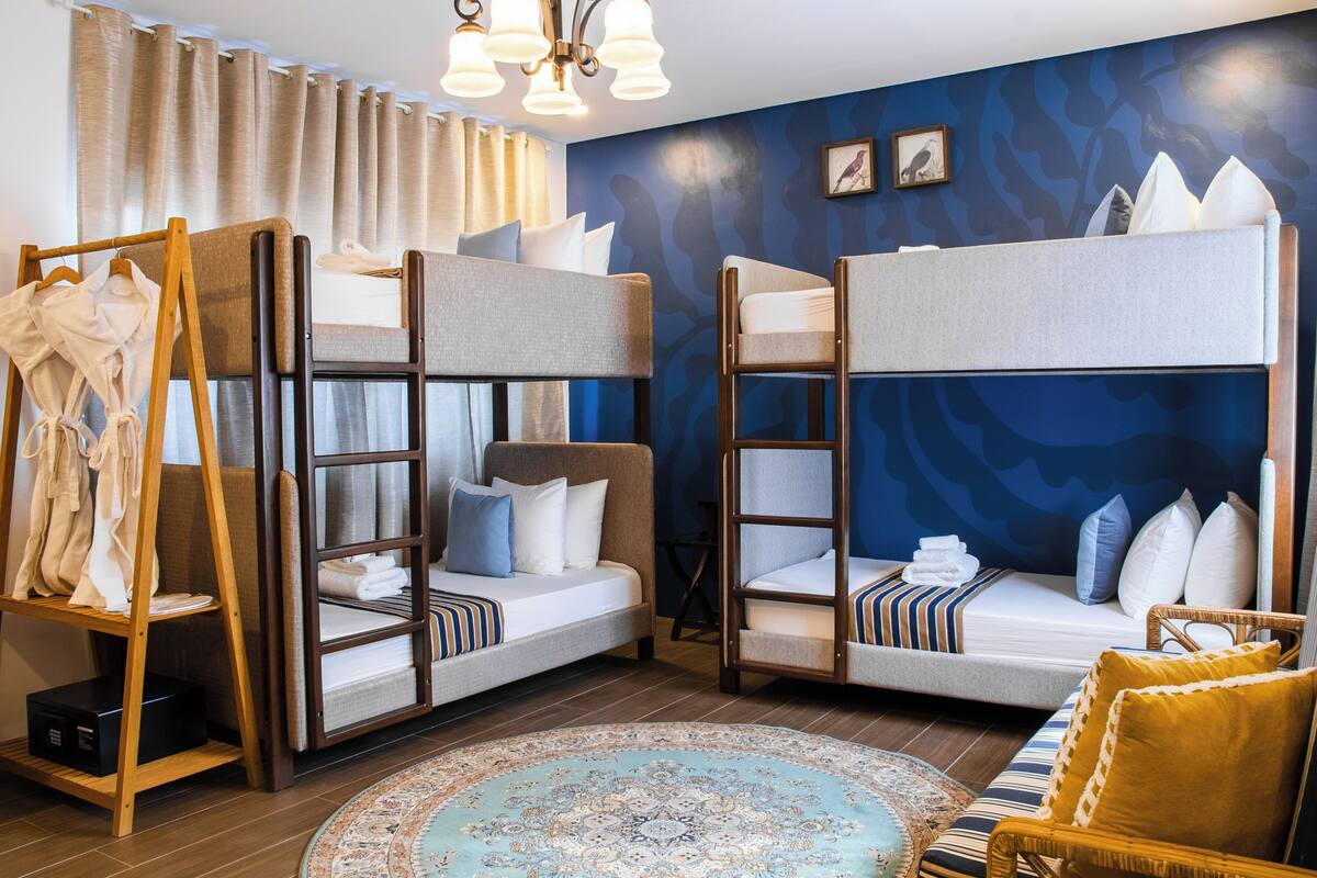 Quarto com beliches, escada de madeira, sofá e tapete estampado.