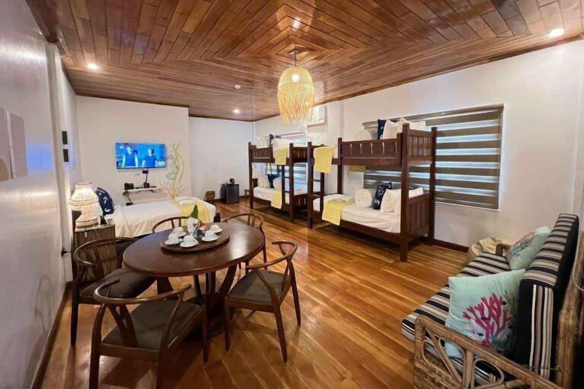 Um quarto acolhedor com teto de madeira, beliches, uma mesa de jantar com cadeiras e um sofá.