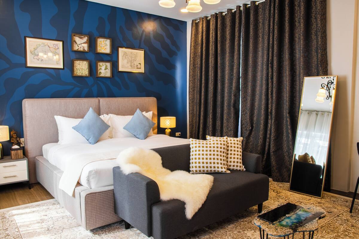 Quarto com cama, mesas de cabeceira, um espelho e uma janela grande com cortinas.