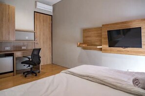Quarto com cama, escrivaninha com cadeira, televisão na parede e guarda-roupa.