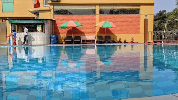 Uma piscina com borda azulejada, um muro de tijolos e dois guarda-sóis.