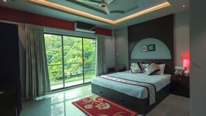 Quarto moderno com uma cama grande, ventilador de teto, tapete vermelho e vista para o verde pela janela.