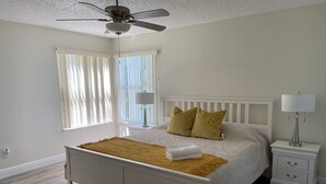 Quarto com uma cama, duas mesas de cabeceira, um ventilador de teto e uma janela com cortinas.