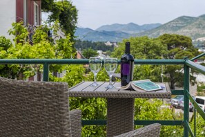 Mesa de vime com dois copos de vinho e uma garrafa, com uma paisagem de montanhas ao fundo.