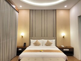 Quarto de hotel moderno com uma cama grande, duas mesas de cabeceira, luminária fixada na parede e cortina.
