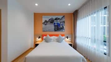Quarto de hotel com uma cama grande, duas mesas de cabeceira com luminárias, um quadro na parede e uma janela com cortinas leves.
