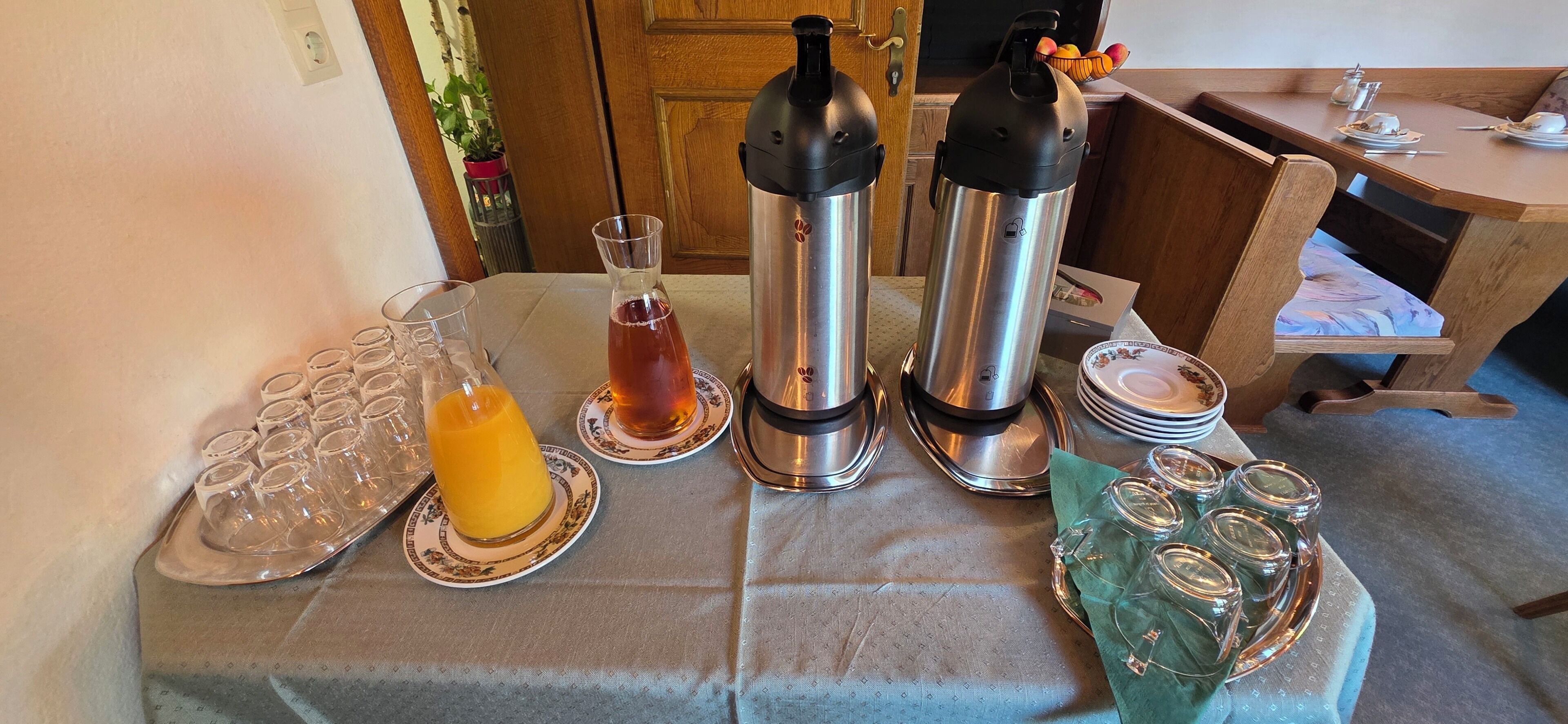 Uma mesa com máquina de café, bule de chá e jarra de sumo de laranja.