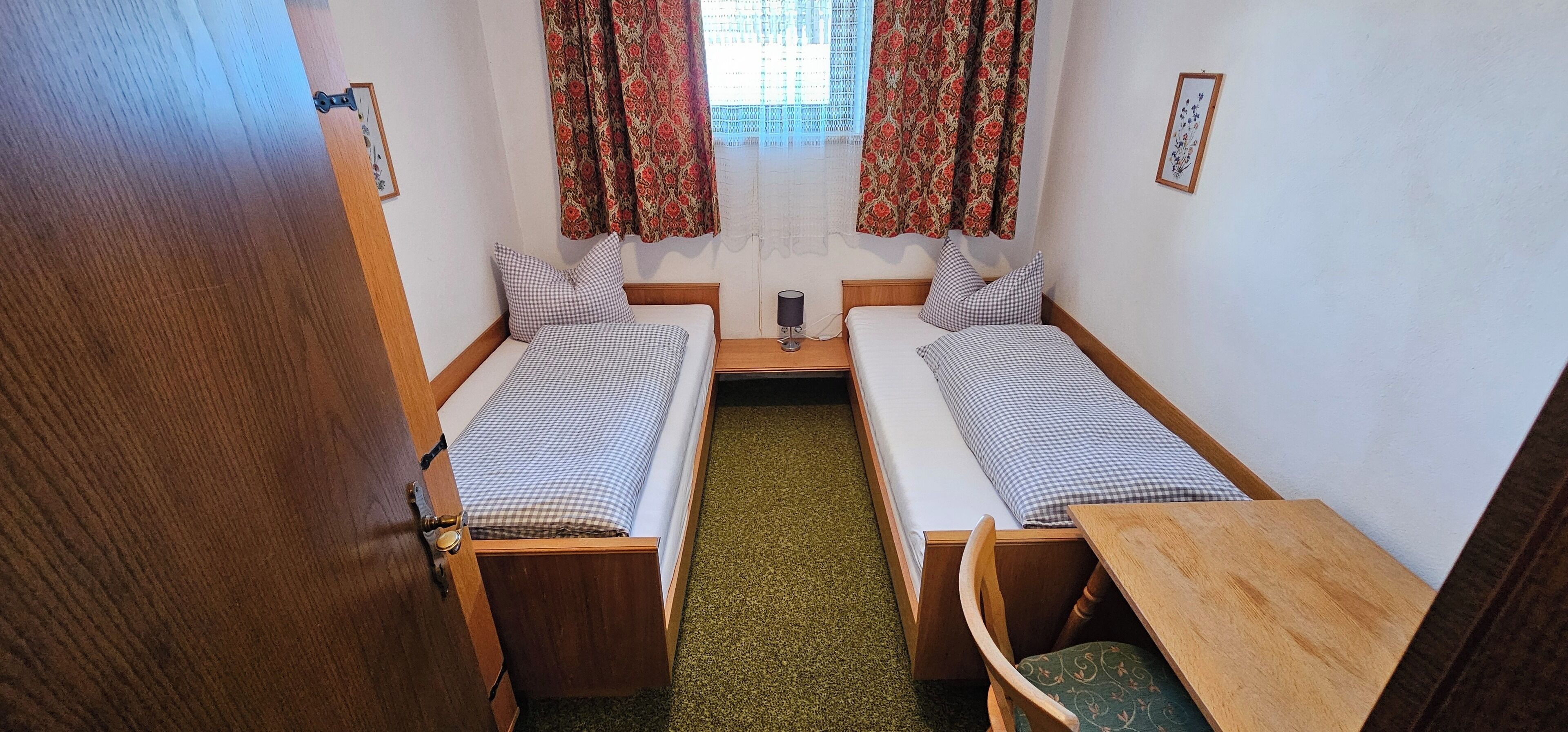 Quarto pequeno e compacto com duas camas de solteiro, uma mesinha e uma cadeira.