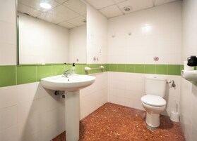 Um banheiro com pia branca, paredes azulejadas em verde, vaso sanitário branco e um espelho.